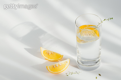 Glass of clean mineral sparkling water with ice and lemon on a white background with sunshine ...