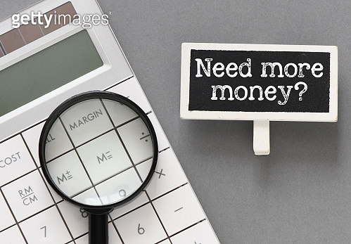 NEED MORE MONEY? words on a small chalkboard next to a calculator and ...