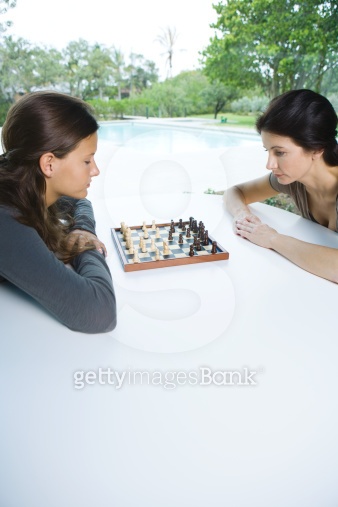 Mother and daughter playing chess together outdoors, side view ...