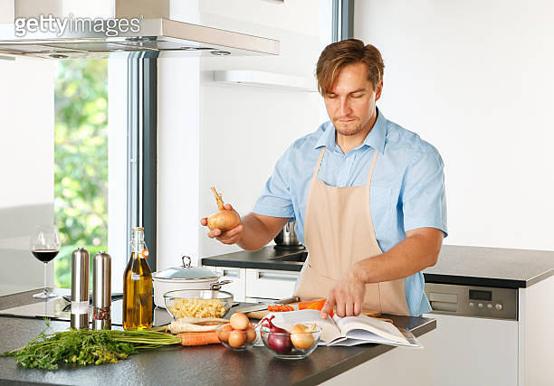 Man cooking in modern kitchen using cookbook (171552896) - 게티이미지뱅크