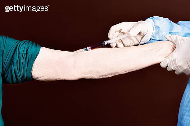 Gloved and gowned medical professional gives old woman injection ...