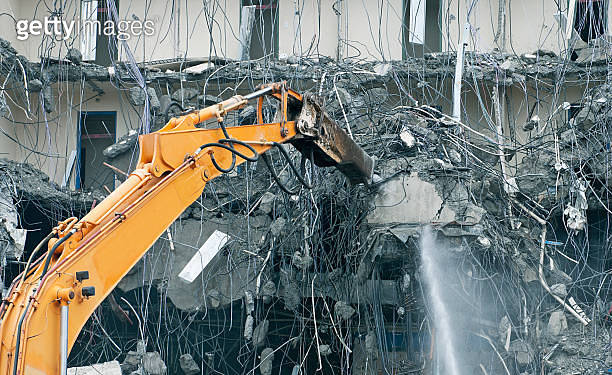 Crane with hammer attachment battering concrete during apartment ...