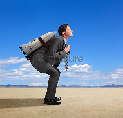 Businessman standing with rocket strapped to his back in desert ...