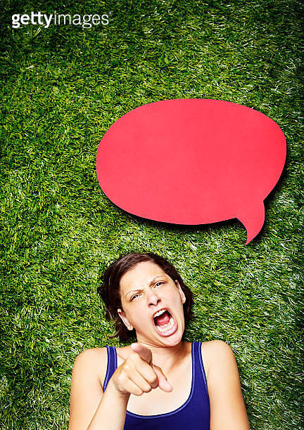Furious young woman points finger accusingly under blank speech bubble ...