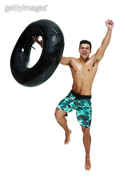 Cheerful young man jumping with inner tube (499891045) - 게티이미지뱅크
