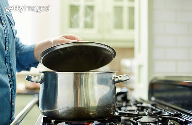 Woman lifting steel lid over cooking pan on stove (481217202) - 게티이미지뱅크