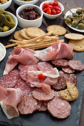Assorted deli meat snacks, sausages and pickles on a blackboard ...