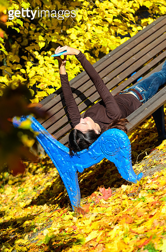 Attractive young woman laying on brown wooden bench with mobile 이미지 ...