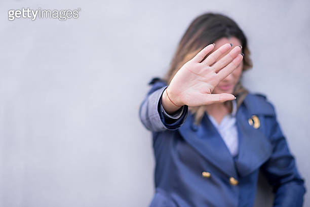 Woman giving hand stop sign while standing against gray wall 이미지 ...