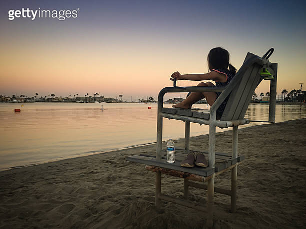 Little girl sitting on lifeguard chair looking at ocean (547217048 ...