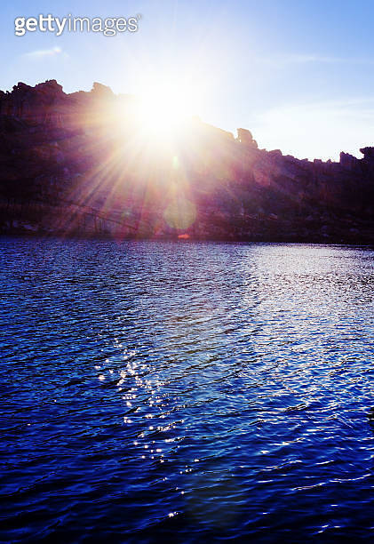 Sun peeping from behind rocks shines over rippling water (530941896 ...