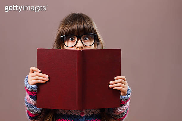 Little girl hiding behind book 이미지 (510017506) - 게티이미지뱅크