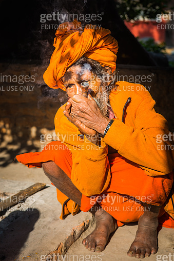 Sadhu holy man traditional saffron robes smoking charas Kathmandu Nepal ...
