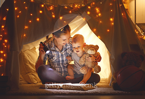 mother and baby son with a book and a flashlight before going to bed ...