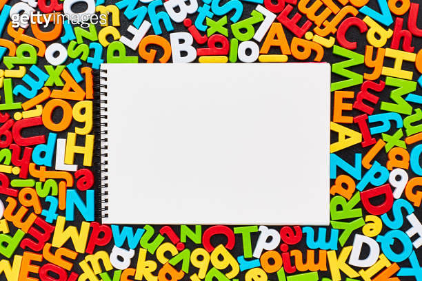 Overhead view of blank spiral book amidst multi colored alphabets ...