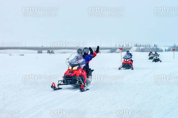 People waving hands and riding snowmobile in frozen lake Rovaniemi ...