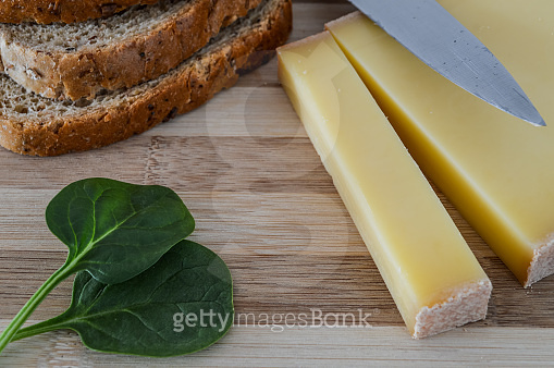 slice of french comte cheese on wood cutting board with fresh green ...