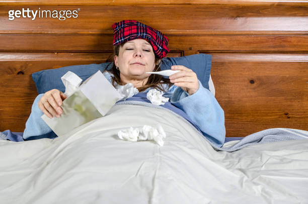 Woman sick in bed with a box of tissues and looking at thermometer 이미지 ...