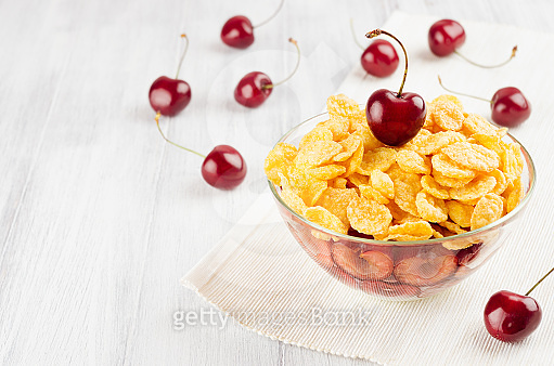Summer breakfast with golden corn flakes, ripe cherries on white wood ...