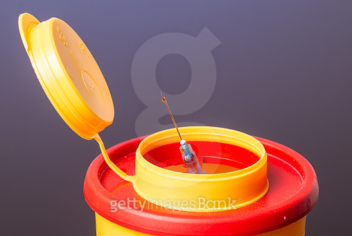 Yellow medical disposal waste box, syringe needle with red drop on the ...
