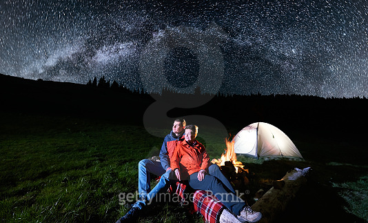 Night camping. Man and woman tourists sitting at a campfire near ...