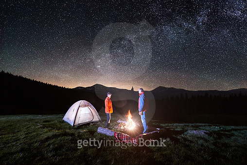 Night camping. Couple tourists standing at a campfire near illuminated ...