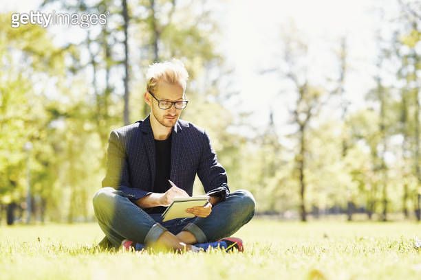 Sitting on lawn male writing in notebook 이미지 (1017543898) - 게티이미지뱅크