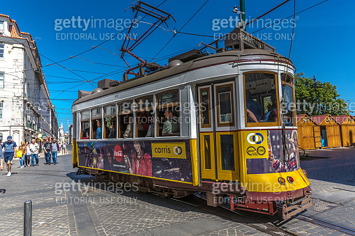 Tourist and locals riding a traditional yellow tram in downtown Lisbon ...