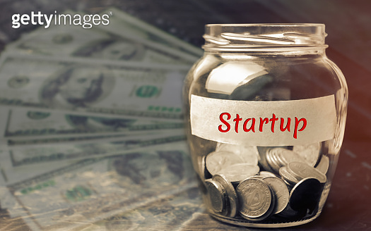 Glass jar with coins and the word ' Startup '. The concept of raising ...