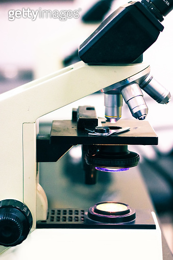 side view of a a light microscope with knobs and screws with light on ...