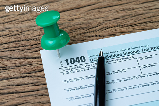 Big green thumbtack pin on 1040 individual income tax form with pen to ...