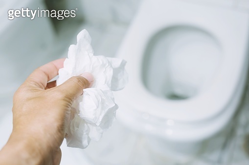 close up hand holding a tissue to be thrown into the toilet bowl. Can ...