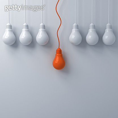Think different concept One hanging orange light bulb standing out from ...