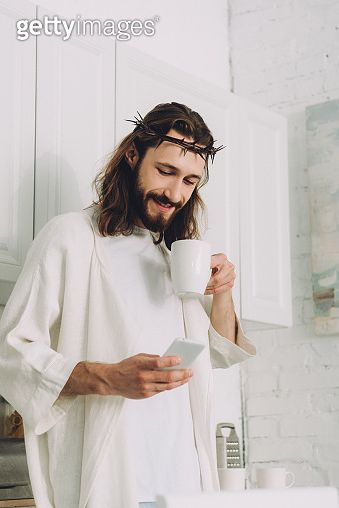 selective focus of Jesus in crown of thorns standing with cup of coffee ...