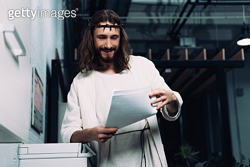 selective focus of smiling Jesus in crown of thorns and robe checking ...