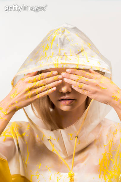 woman in raincoat painted with yellow paint covering eyes with hands ...