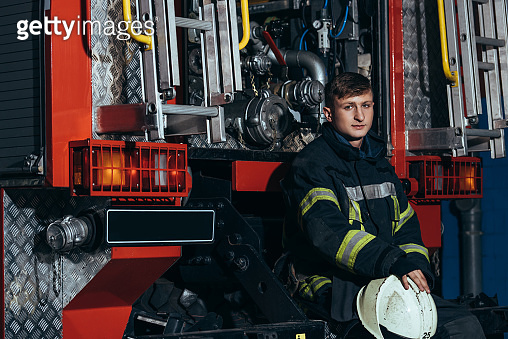 portrait of male firefighter with protective helmet in hands at truck ...