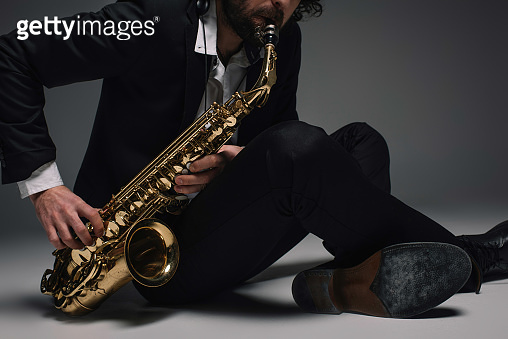 cropped shot of musician playing saxophone while sitting on floor 이미지 ...