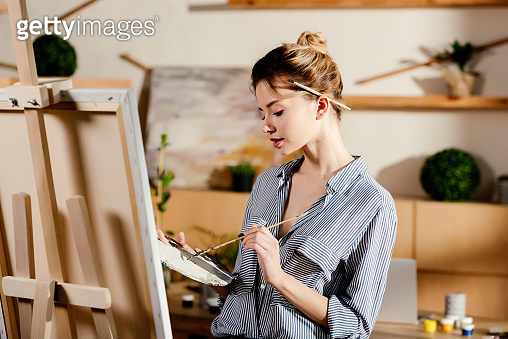 female artist with paintbrush behind ear drawing picture in studio ...