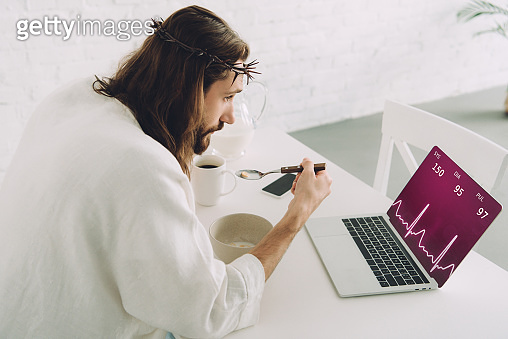 concentrated Jesus eating corn flakes on breakfast at table with laptop ...