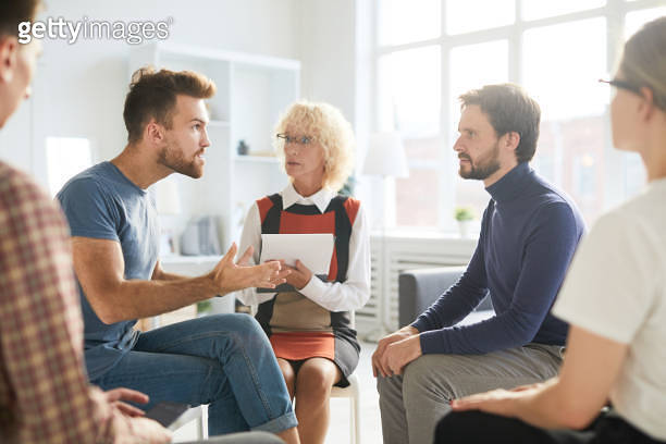 Aggressive displeased young man in jeans sitting on chair and gesturing ...