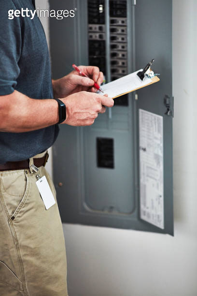 Male electrical engineer wearing a fitness tracker checking fuse box ...