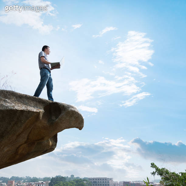 Man standing at the edge of a cliff using laptop 이미지 (957332028) - 게티이미지뱅크