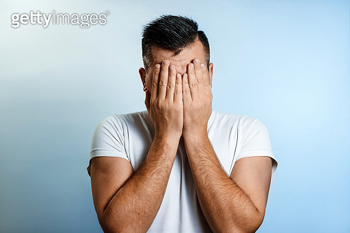 Close-up portrait of a man, covering his face with his hands. On a ...