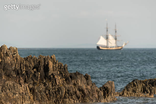 Jagged rocks by the coast with sailing ship on horizon 이미지 (1007649056 ...