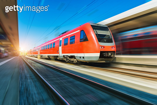 High speed red train in motion on the railway station at sunset. Modern ...