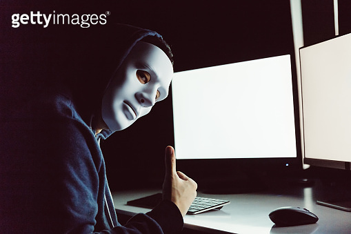 Masked and anonymous hacker under hood giving thumbs up while using a ...