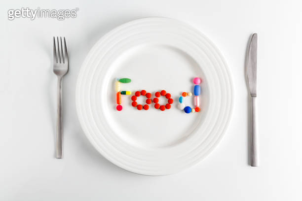 A dinner plate assorted pills and capsules forming food word or sign ...