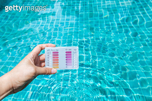 Water testing test kit in girl hand over crystal clear swimming pool ...
