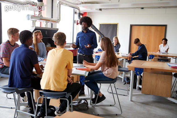 Group Of High School Students Sitting At Work Benches Listening To ...